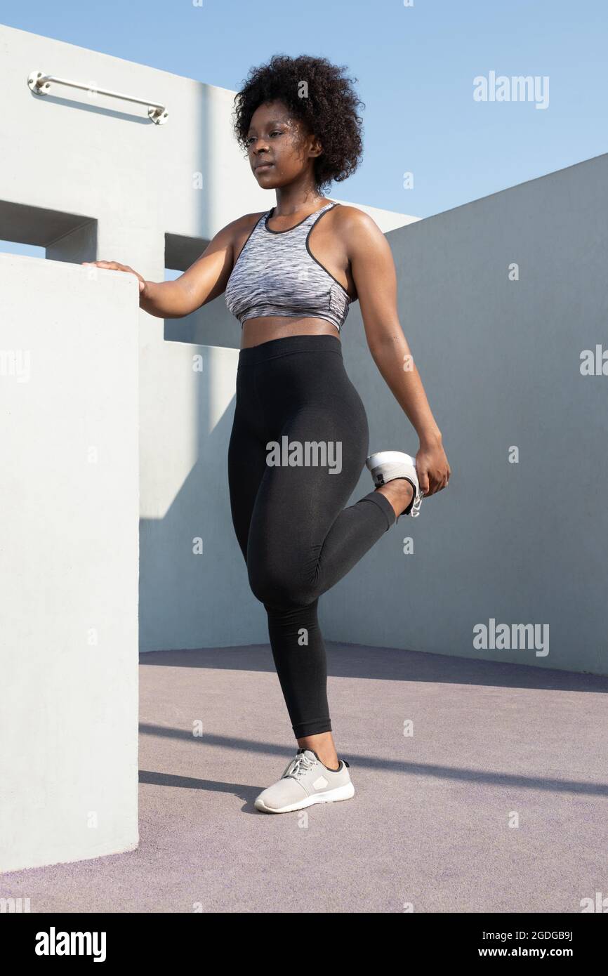 African American sportswoman bending and stretching leg near wall ...