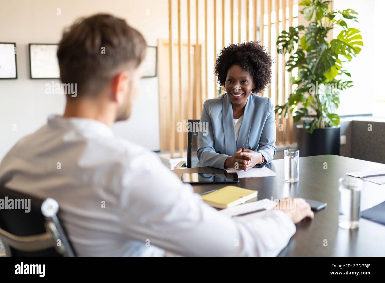 Glad black boss smiling and speaking with male employee during job ...