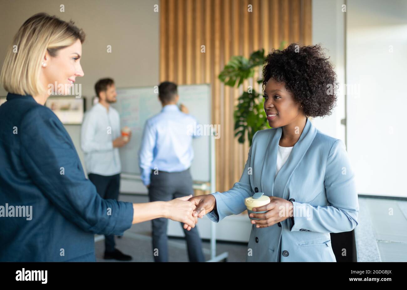 Diverse female managers smiling and shaking hands while striking deal ...