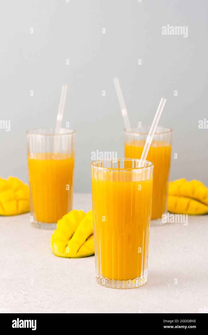 Freshly squeezed mango juice in glasses with a straw, ripe cut mango on ...