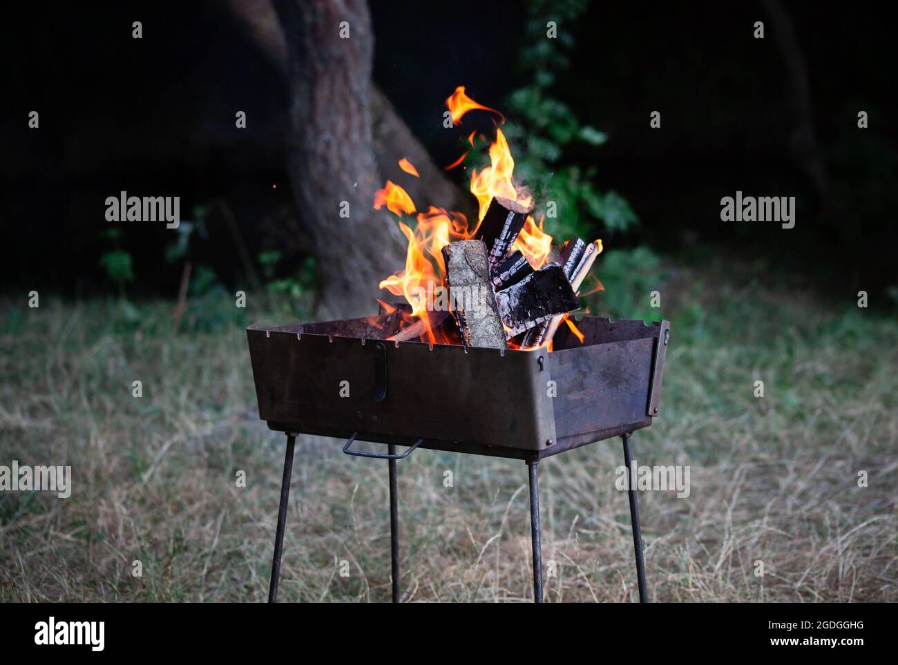 A small folding portable brazier filled with burning wood. Cooking on ...