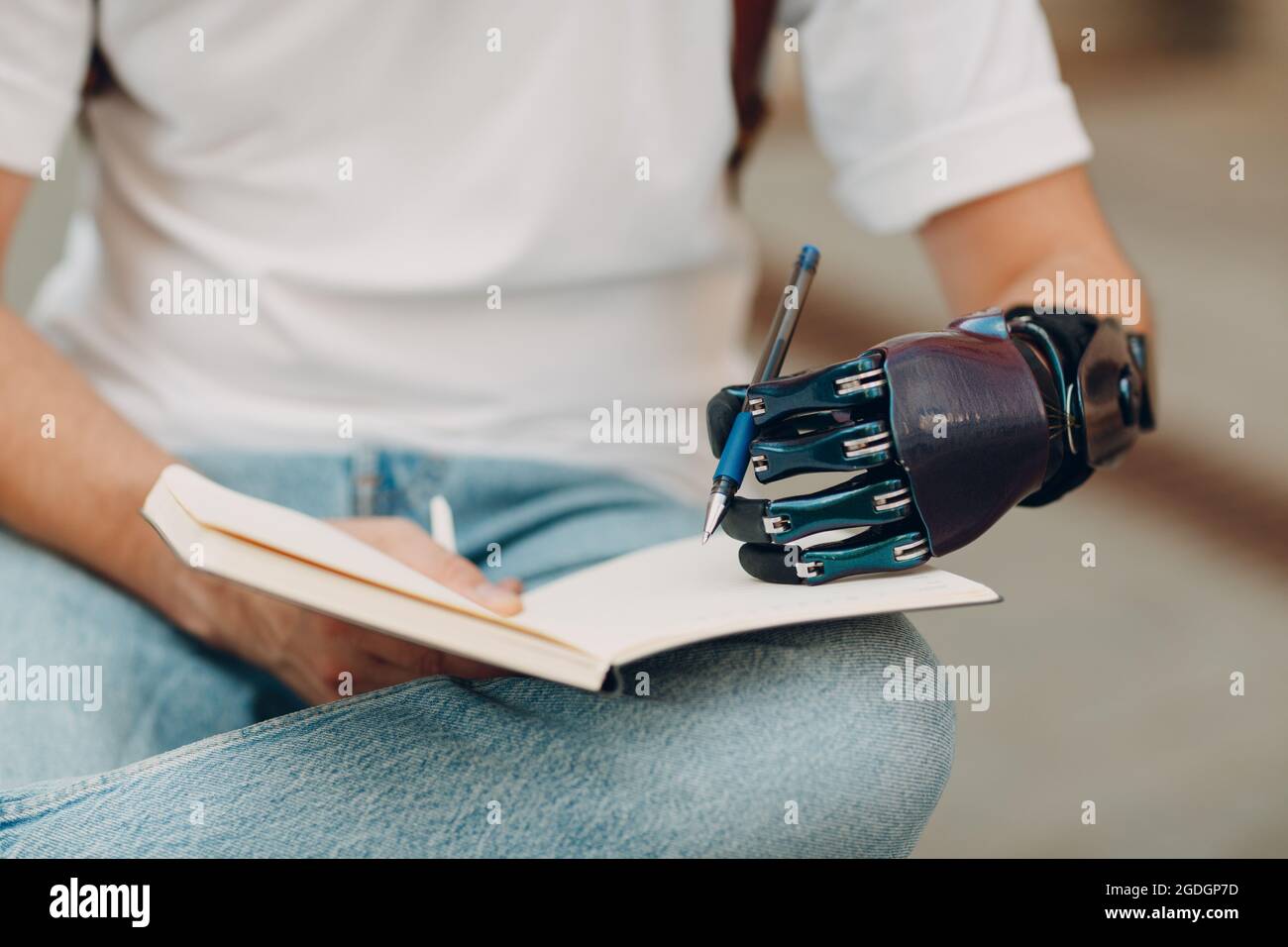 Young disabled man writes in notebook with pen in artificial prosthetic ...