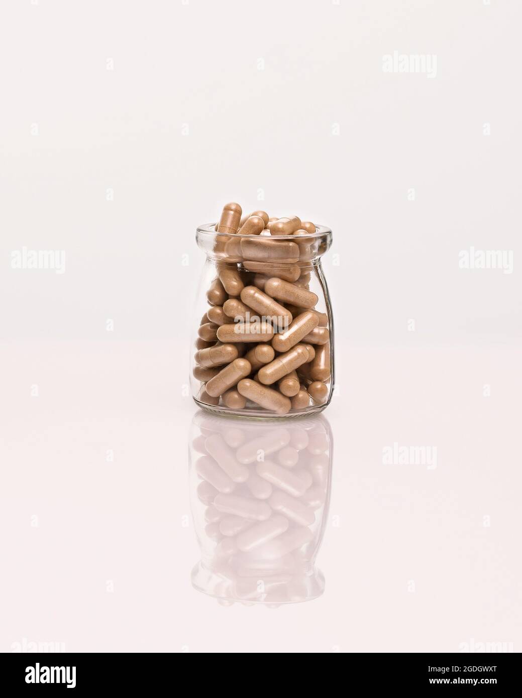 Organic herb capsules in a glass bottle on a white table with ...