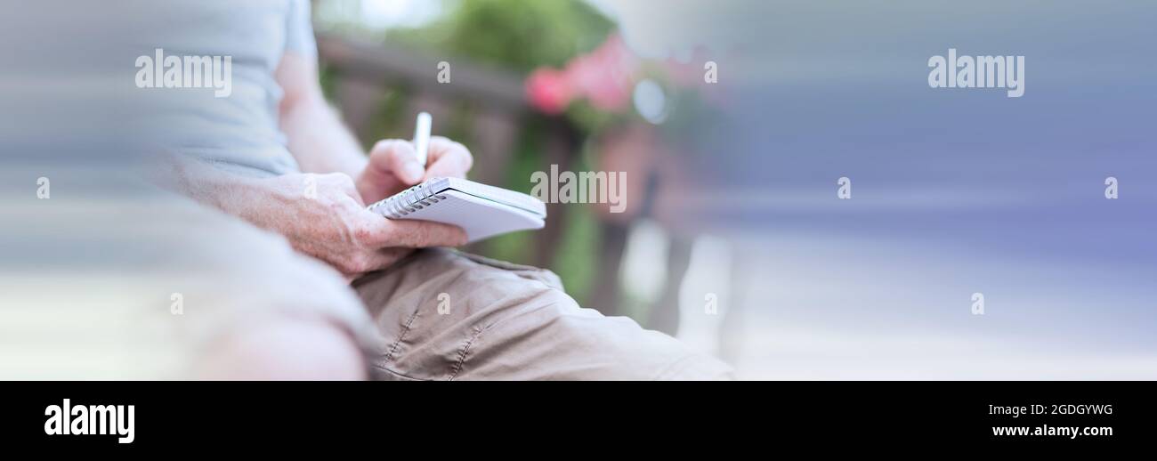 Man sitting outdoor taking notes on a pocket book. panoramic banner ...