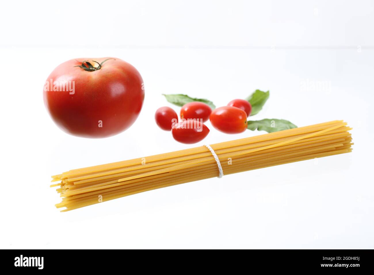 Raw spaghetti noodle with tomatoes and basil isolated in white ...
