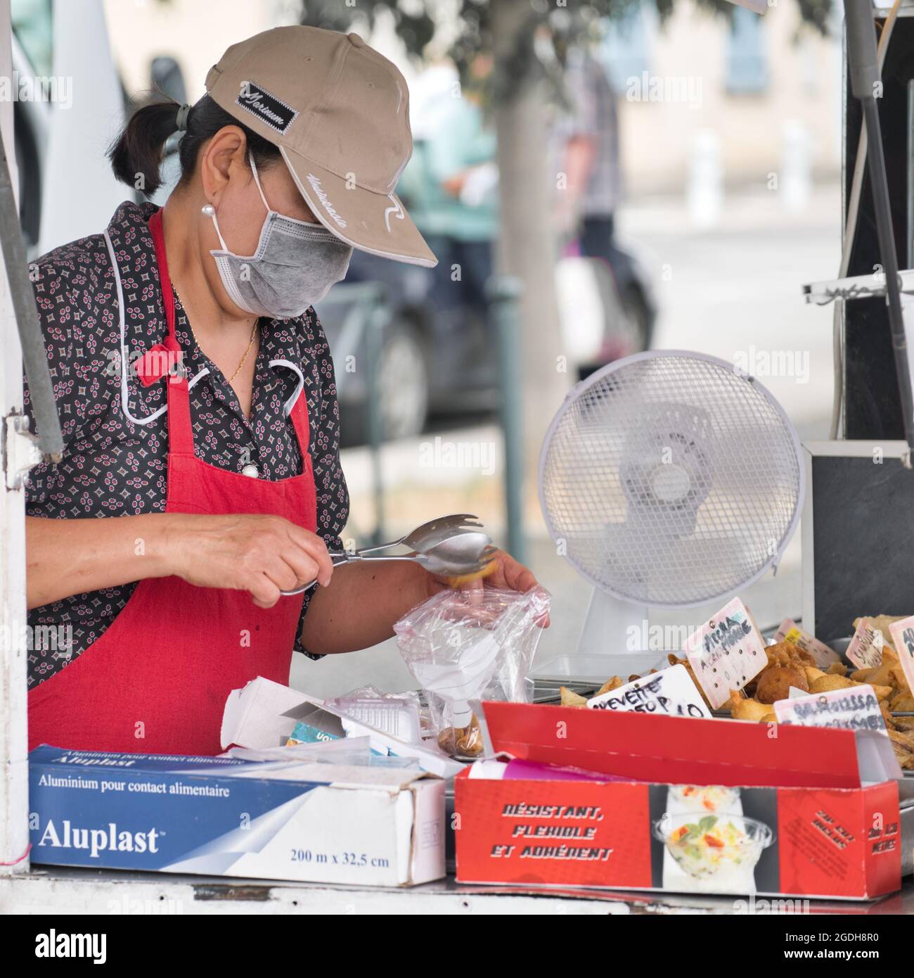 Limoux Aude France 08.13.21 Young woman market vendor wearing red apron ...