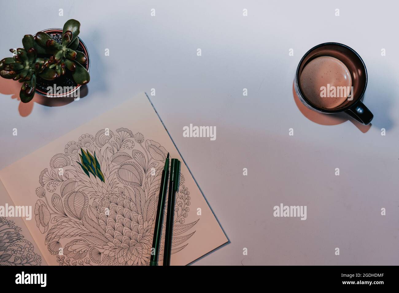Top view of the coloring book, pencils, a small plant , and a glass of ...