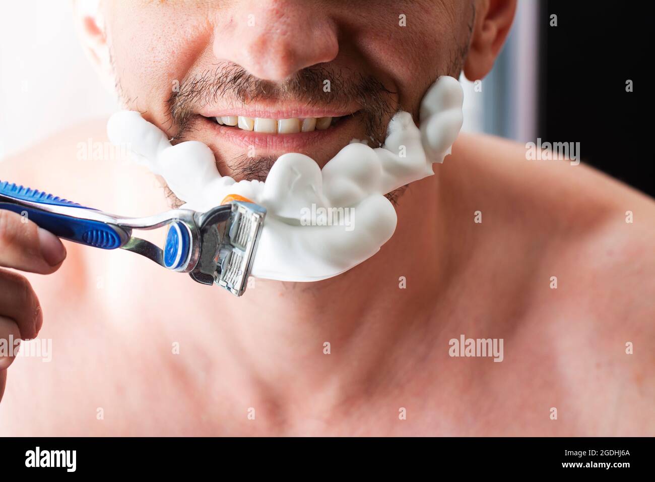 Handsome smiling man shaving his beard with razor in bathroom. Daily ...