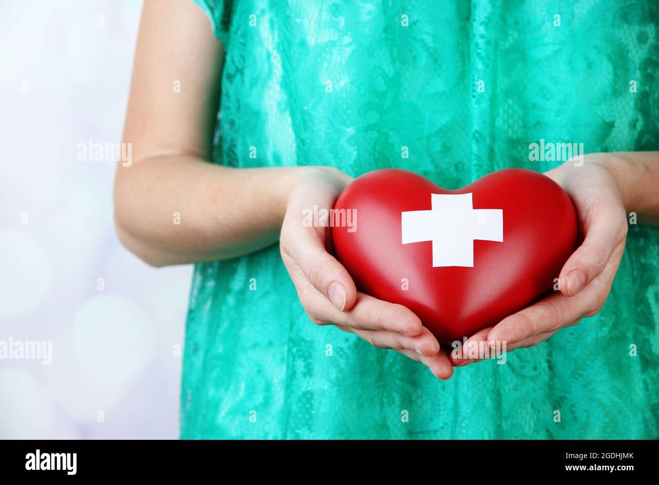 Red heart with cross sign in female hand, close-up, on light background ...