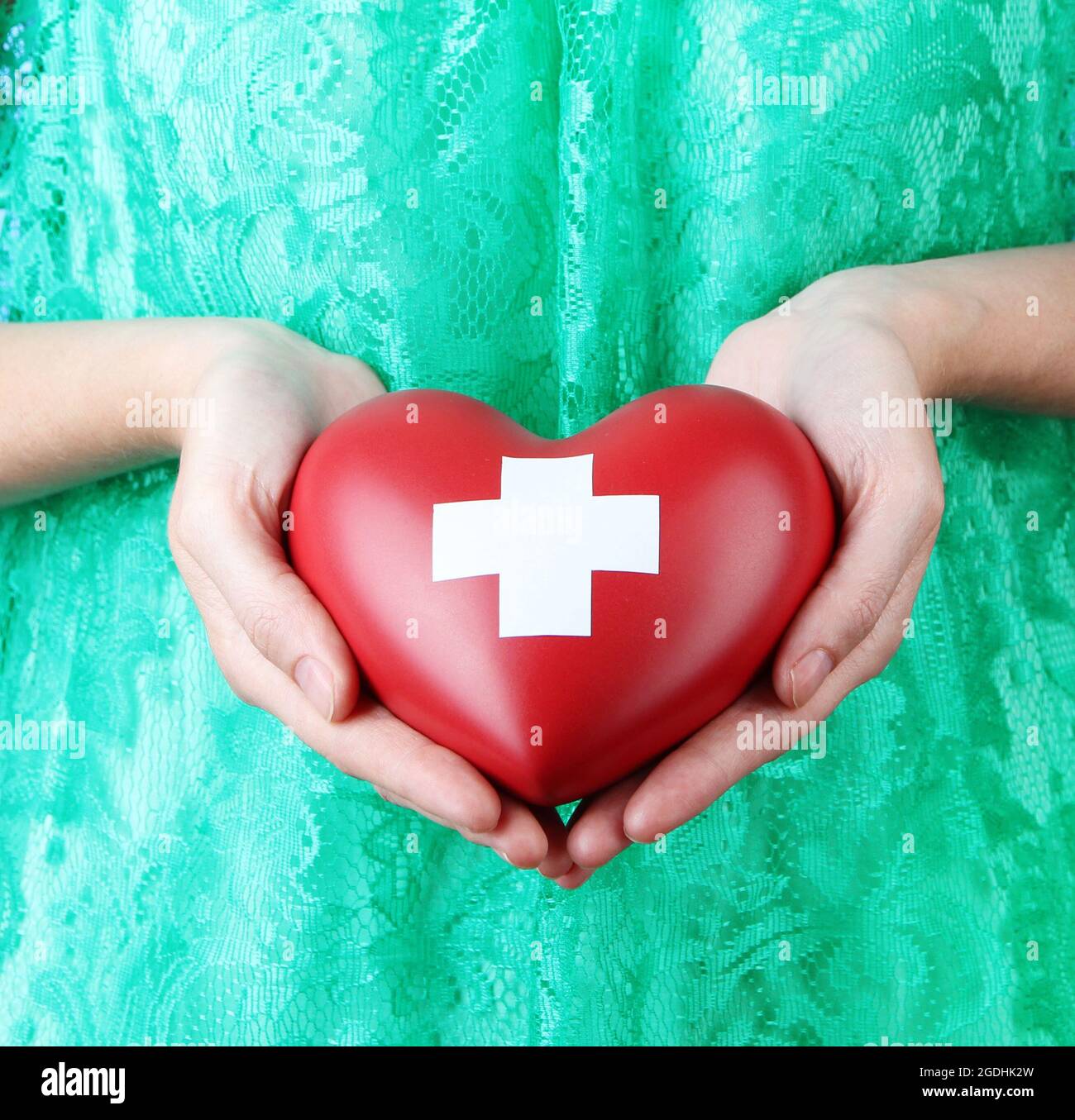 Red heart with cross sign in female hand, close-up, on color background ...