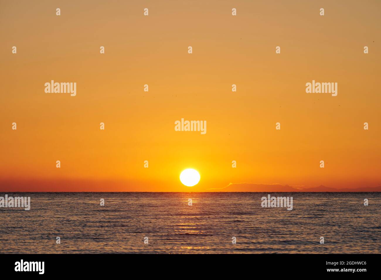 Bright sun rising on cloudless orange sky over rippling sea water in ...