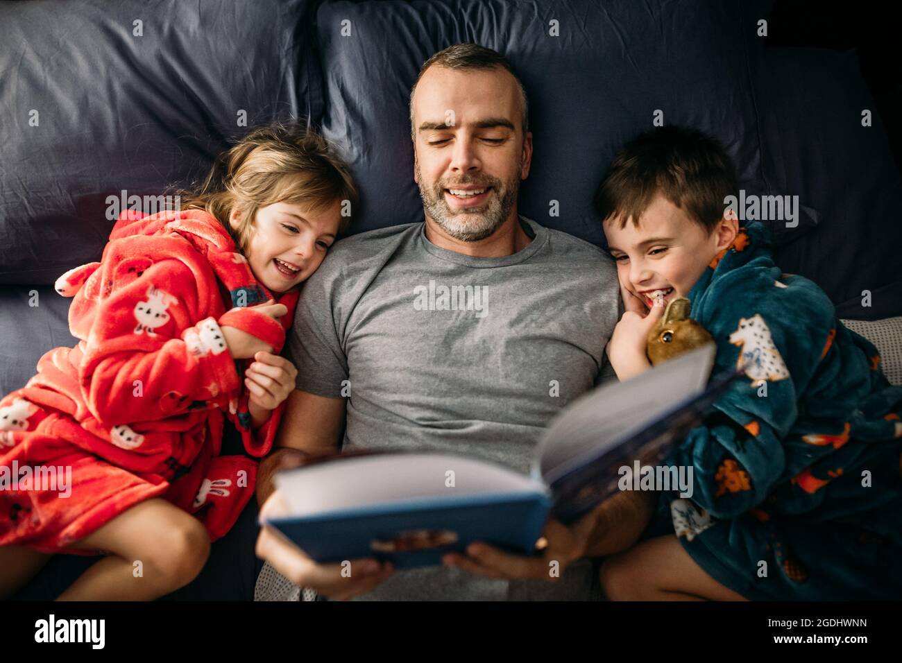 Father reading a book to his children in the master bedroom at night ...