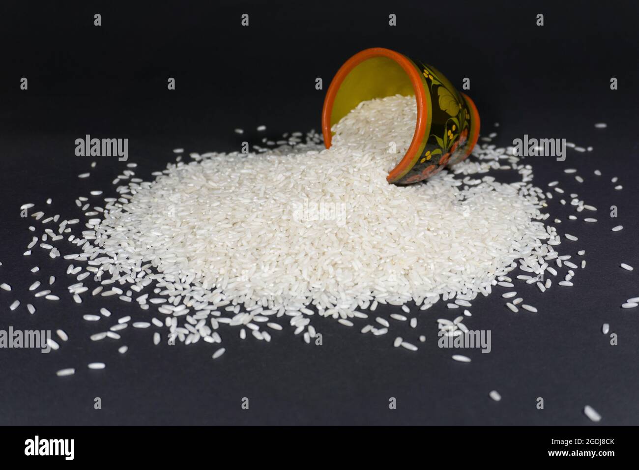 Scattered rice uncooked grains with painted wooden cup on a black ...