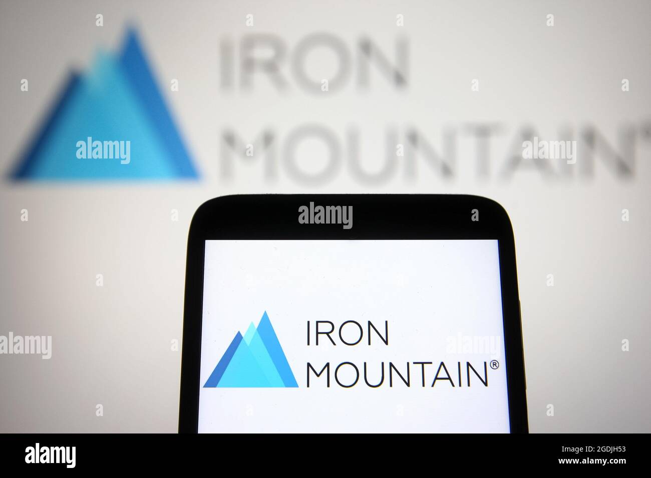 In this photo illustration an Iron Mountain logo is seen on a smartphone and a pc screen Stock ...