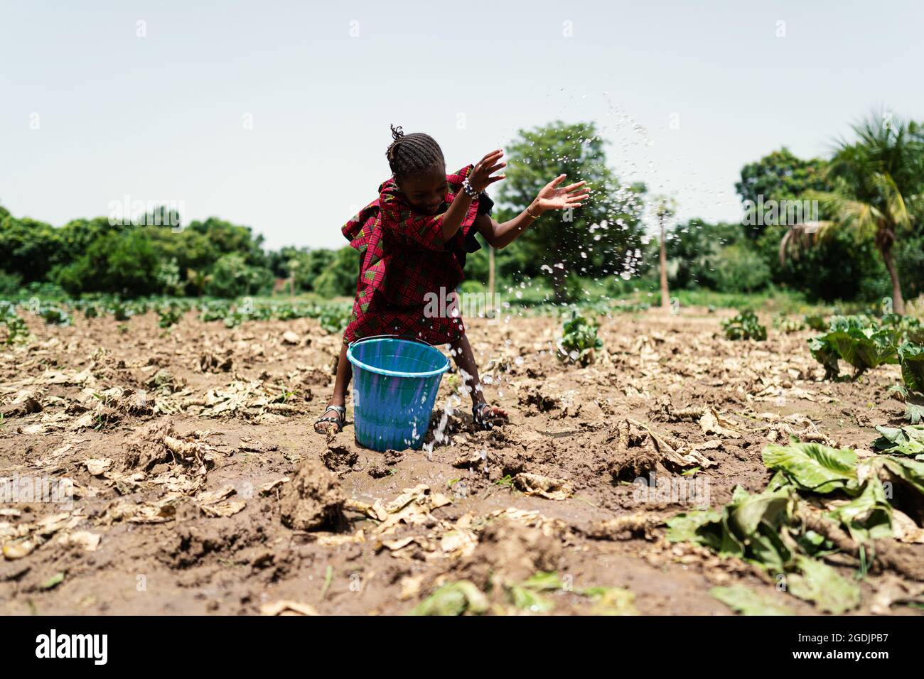 Joyful little African girl throwing water left and right on a dried out ...