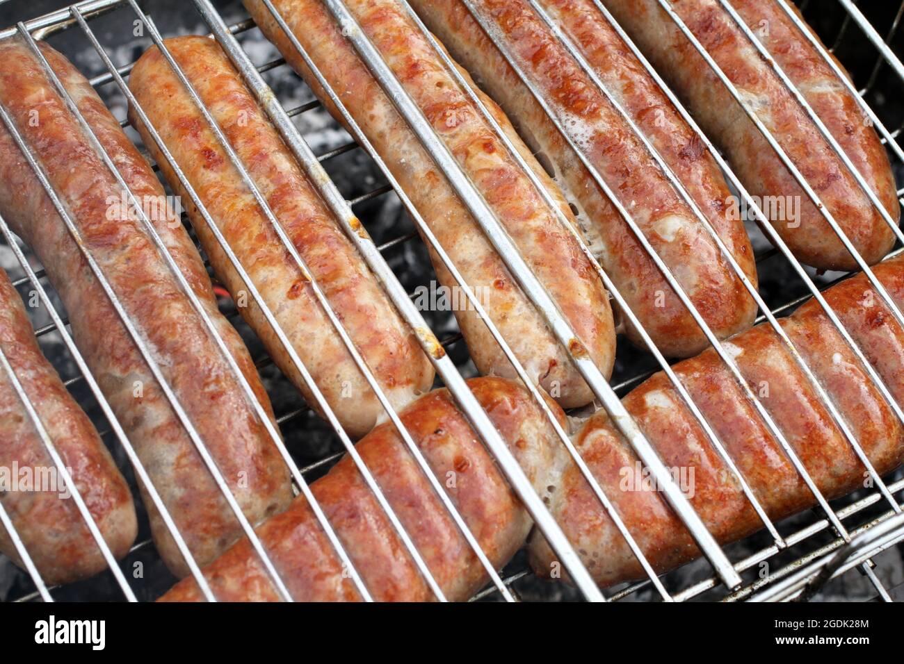 Meat sausages squeezed between grill grates, frying on a grill brazier ...