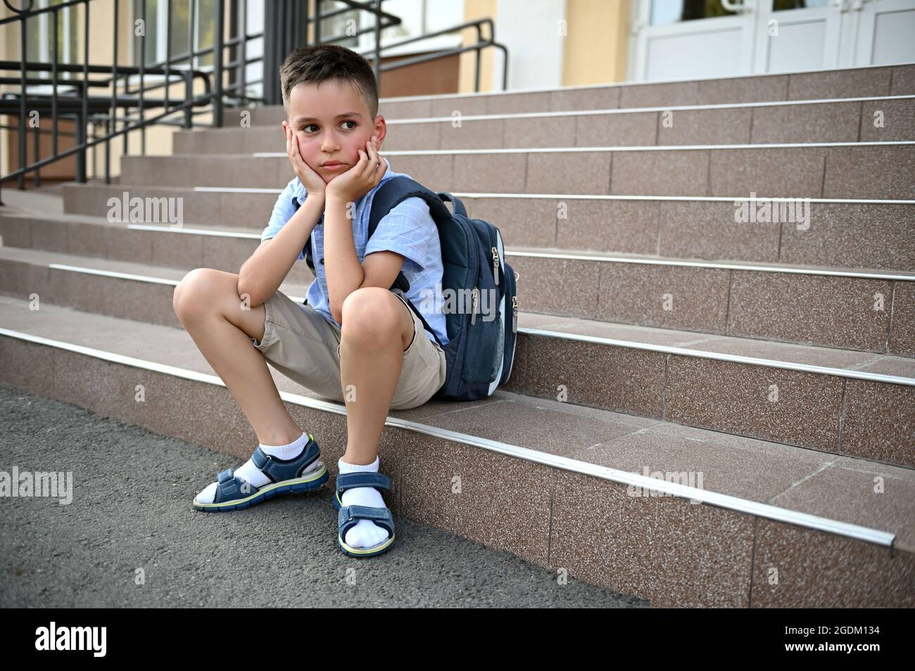 Upset worried boy with backpack sitting on the stairs by school ...