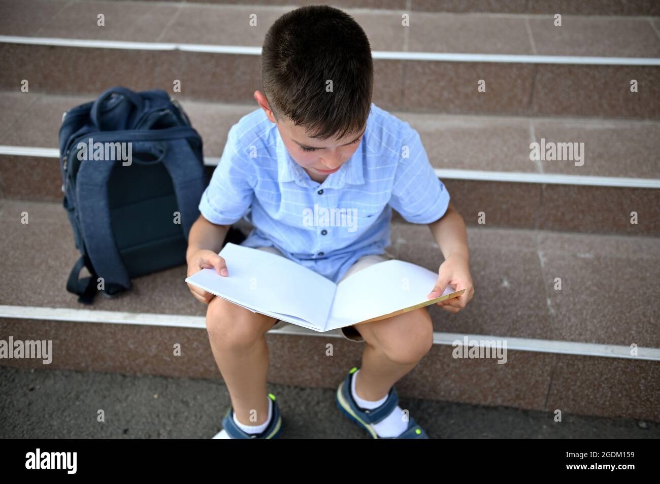 Elementary student doing homework sitting next to his school bag on the ...
