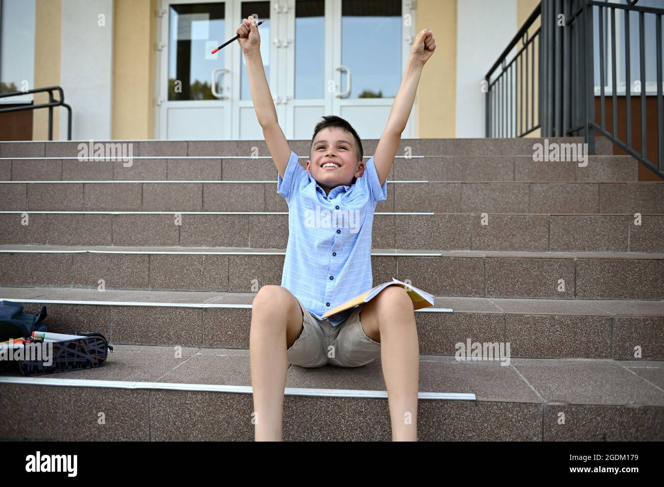Happy elementary student raising his arms up with pencil in hand, feels ...