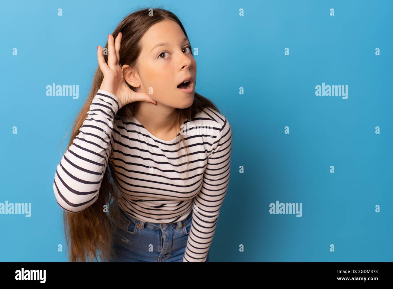 Young caucasian girl in striped shirt making the listening gesture ...