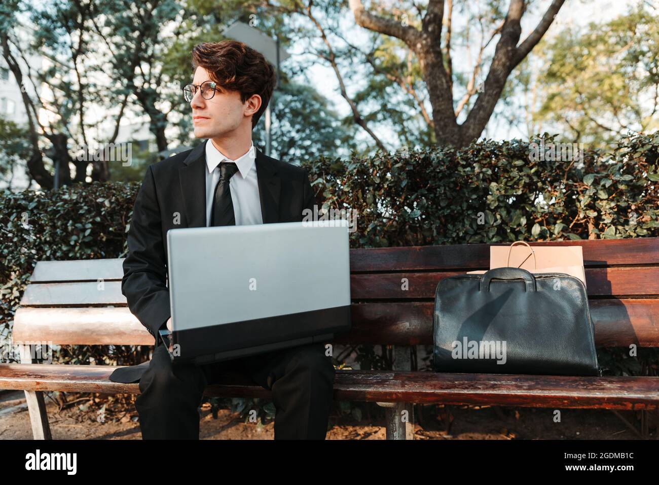 Serious young Caucasian guy dressed professionally sitting on a bench ...