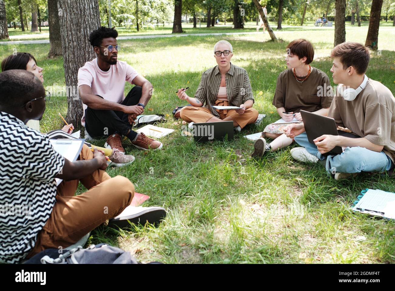 Group of students sitting on the grass and listening to their teacher ...