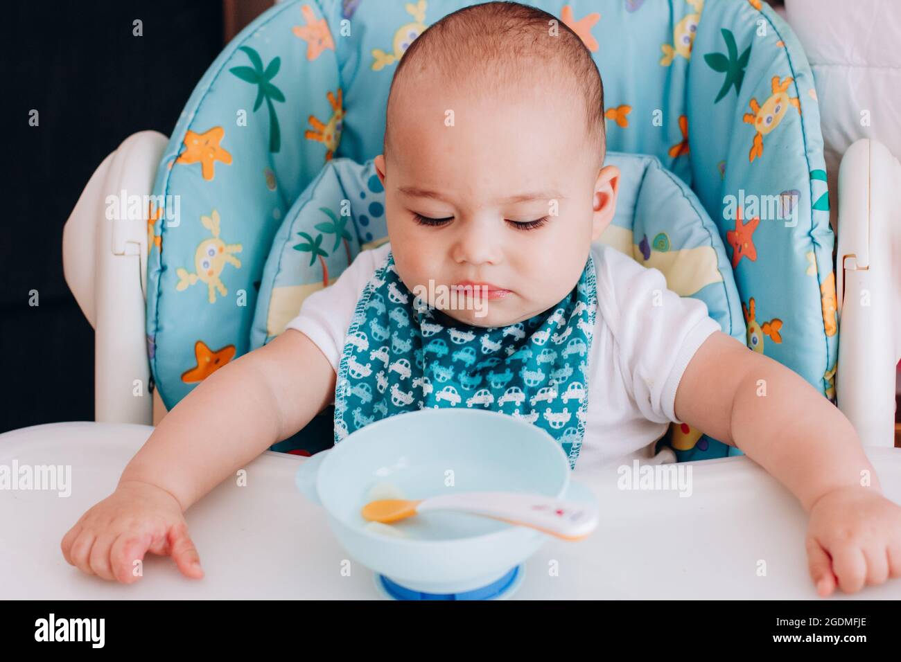 Serious baby sits at baby chair and looking to empty plate. Baby ...