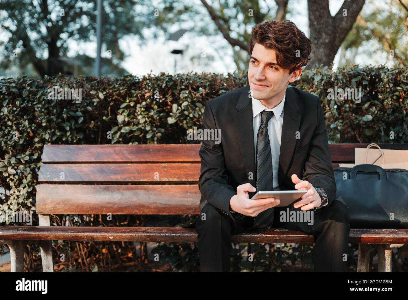 Cheerful professional Caucasian guy sitting on a bench using his tablet ...