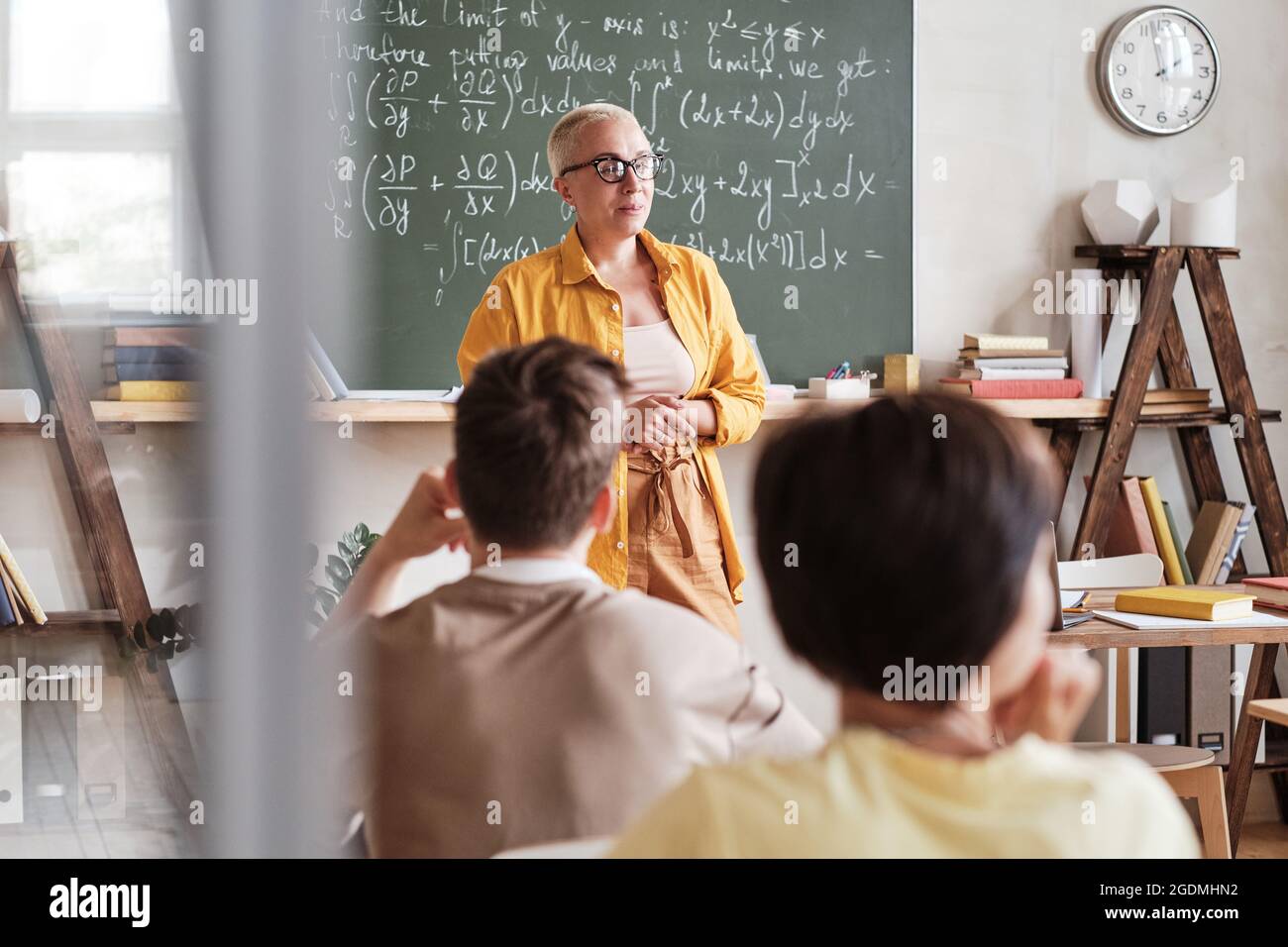 Maths teacher standing at blackboard and explaining material to ...