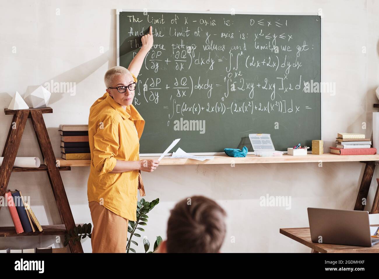 Teacher standing at the blackboard and pointing at math formula she ...