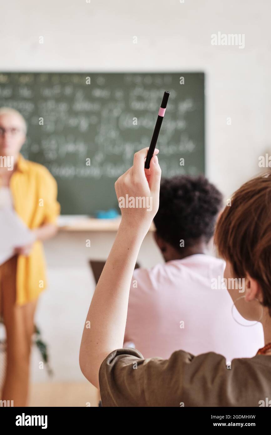 Rear view of student raising her arm up and answering during lesson at ...