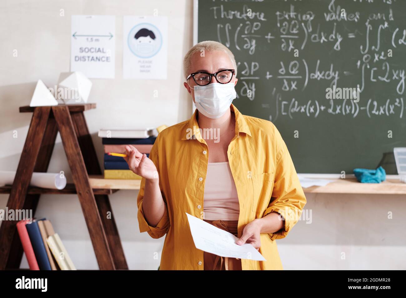 Portrait of young teacher in protective mask explaining new material ...