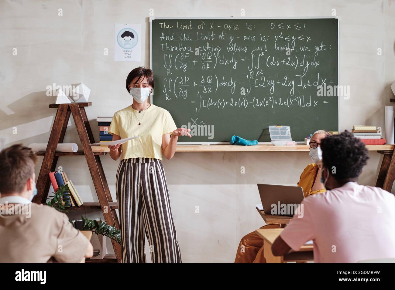 Student in mask standing near the blackboard and passing an exam, she ...