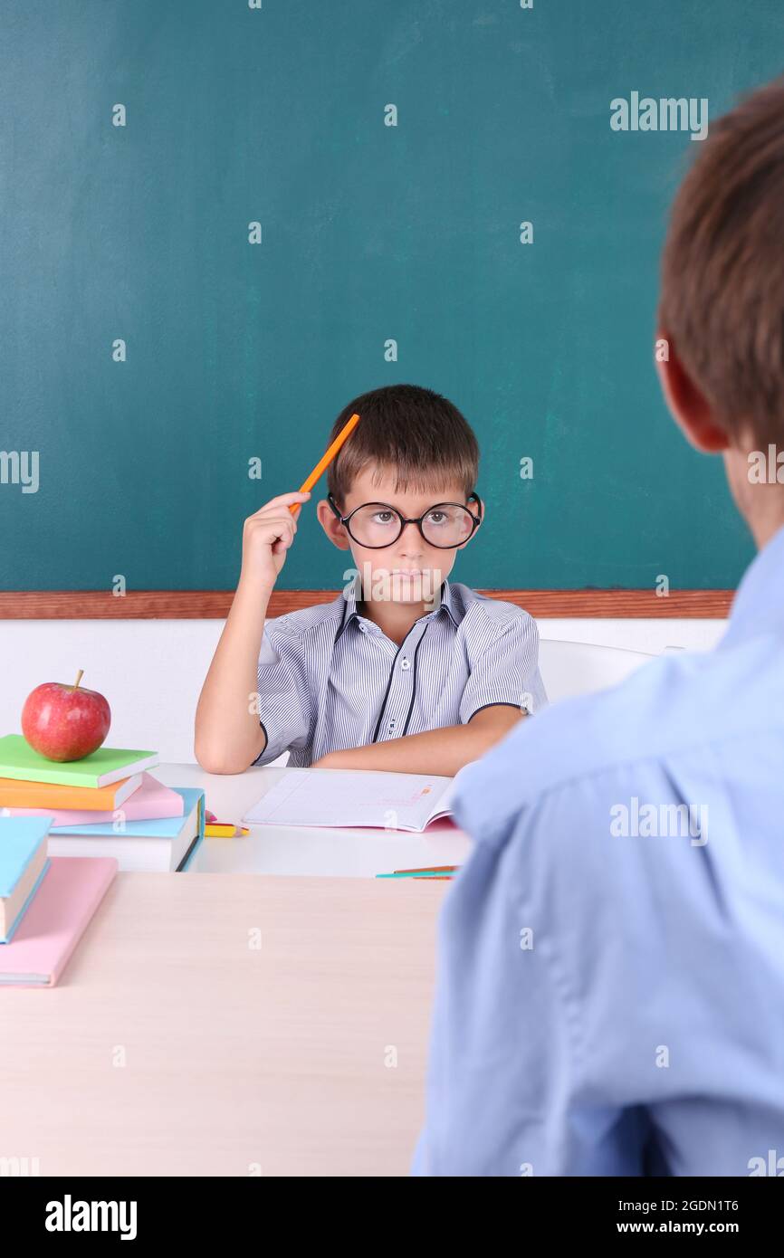 Schoolboy and teacher sitting in classroom on blackboard background ...