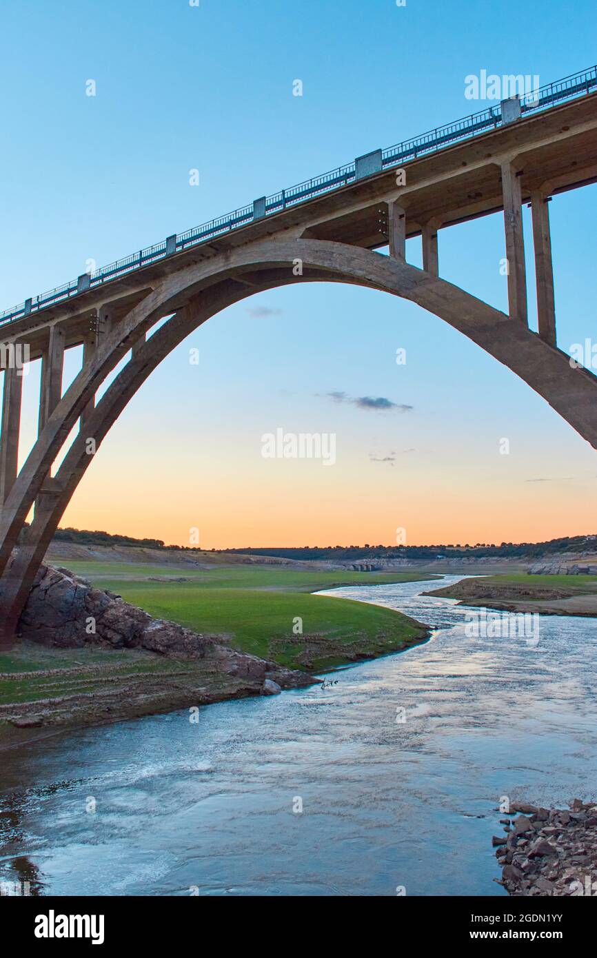 Very big and high stone bridge over a small river with a sunset sky ...
