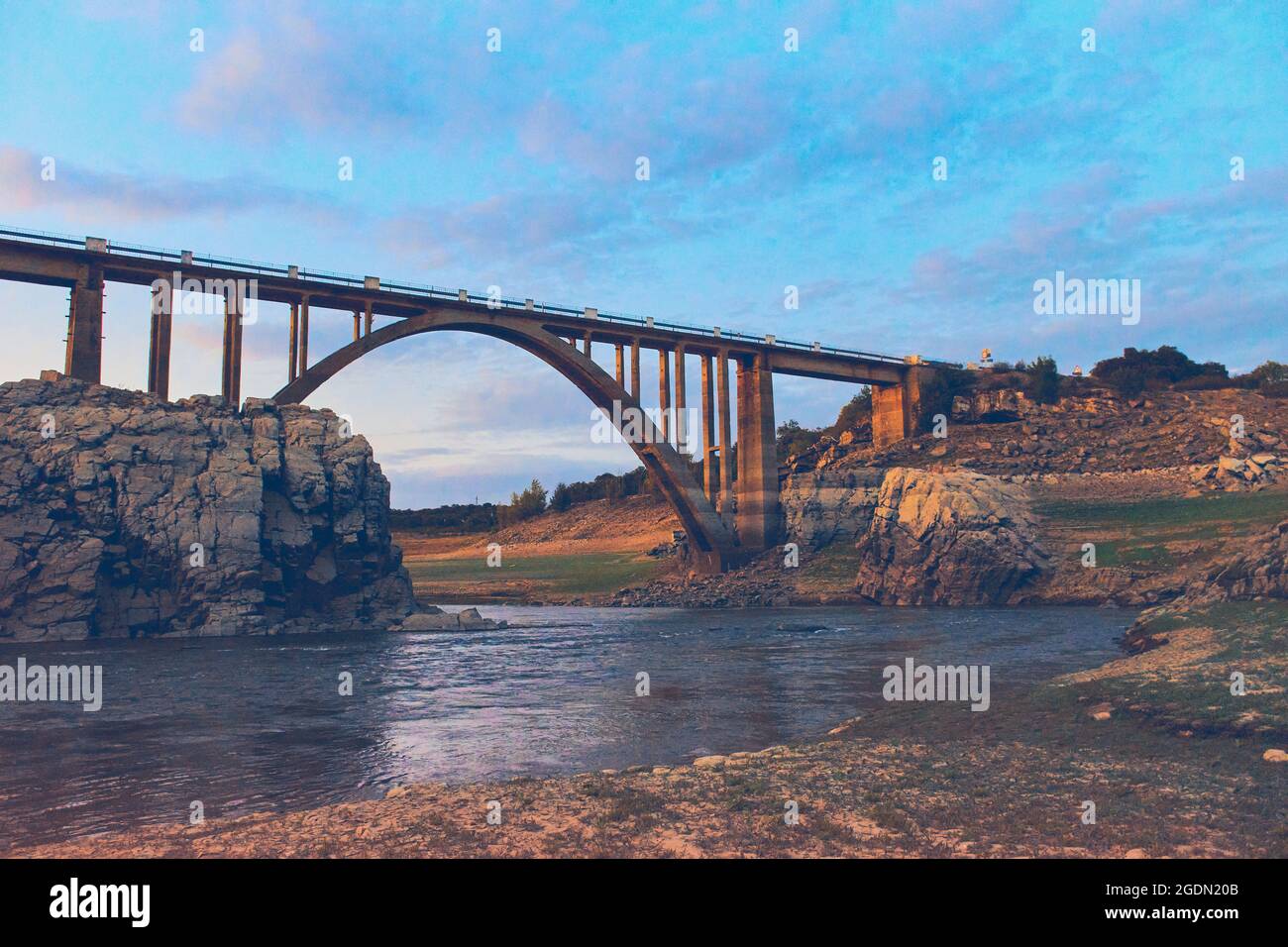 Very big and high stone bridge over a small river with a sunset sky ...