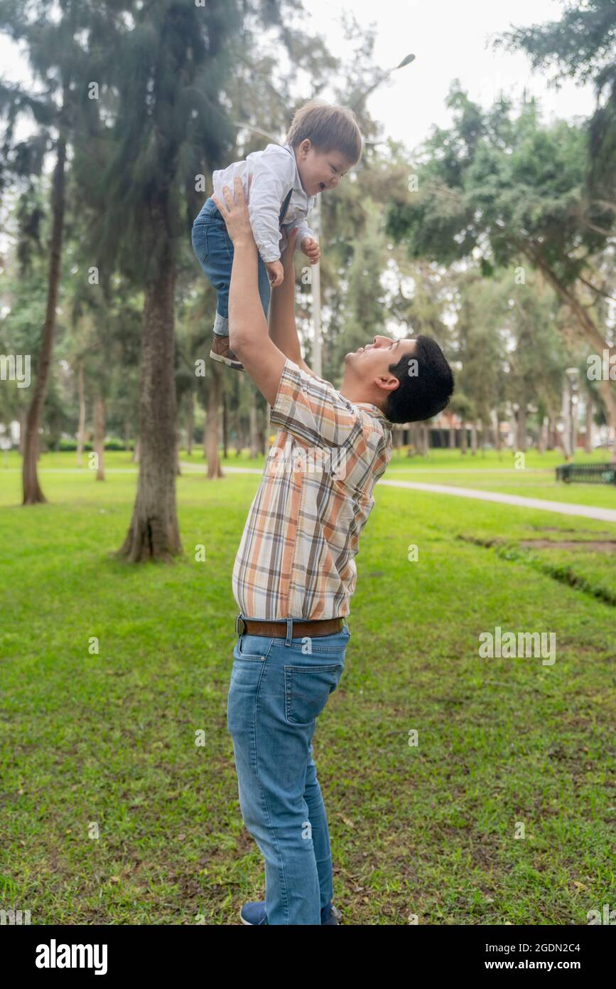 Vertical photo of a father raising her child in mid-air as they laugh ...