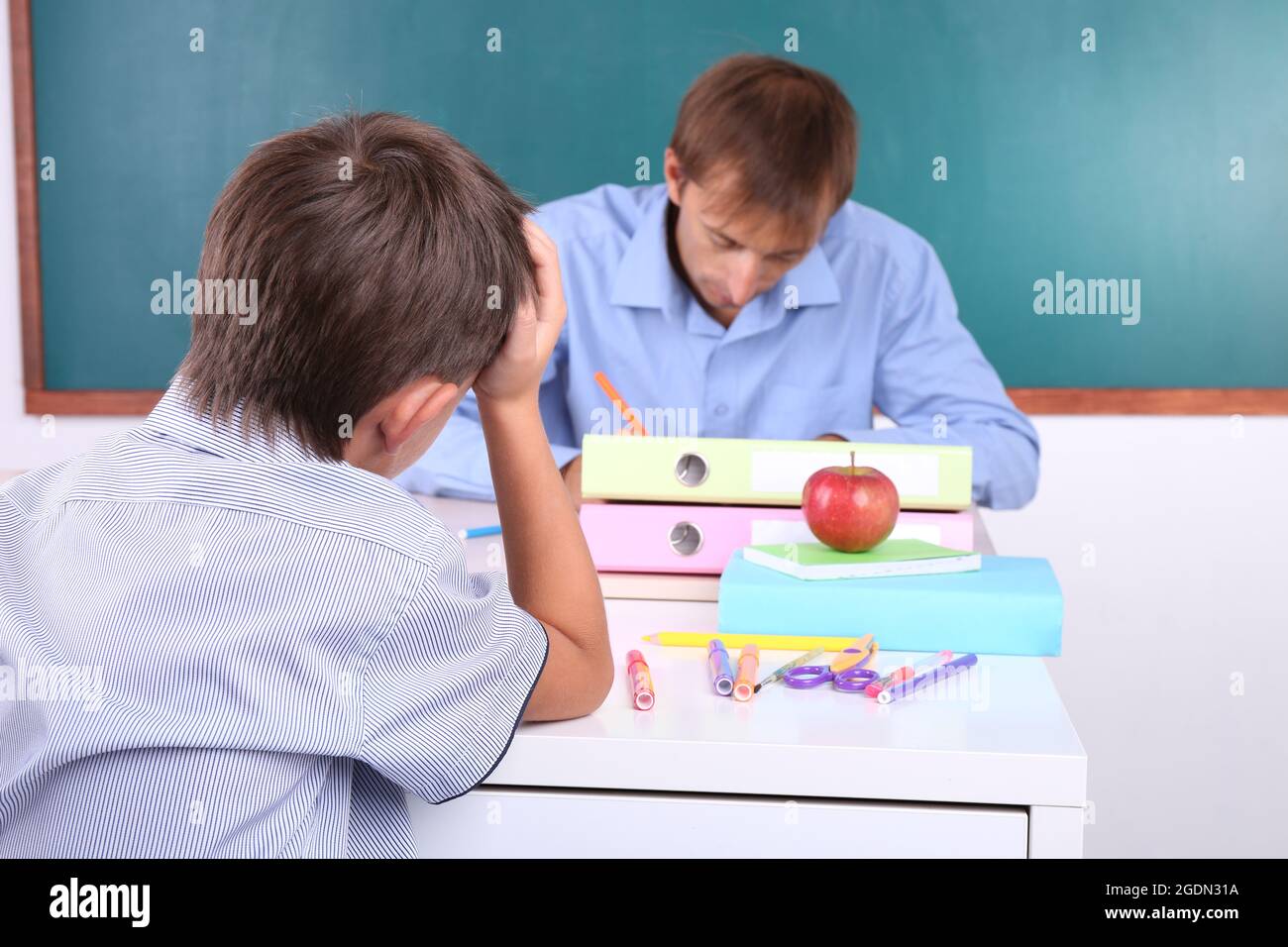 Schoolboy and teacher sitting in classroom on blackboard background ...