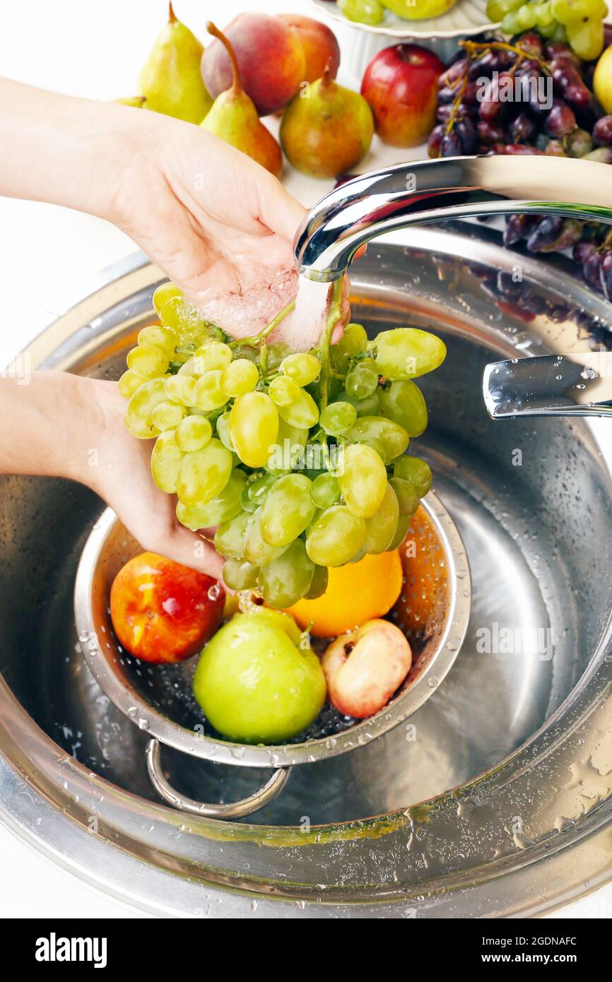 Woman's hands washing grapes and other fruits in colander in sink Stock Photo - Alamy