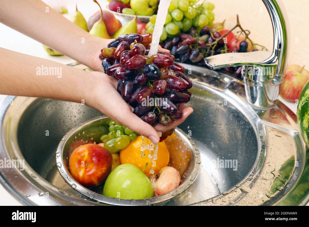 Woman's hands washing grapes and other fruits in colander in sink Stock Photo - Alamy