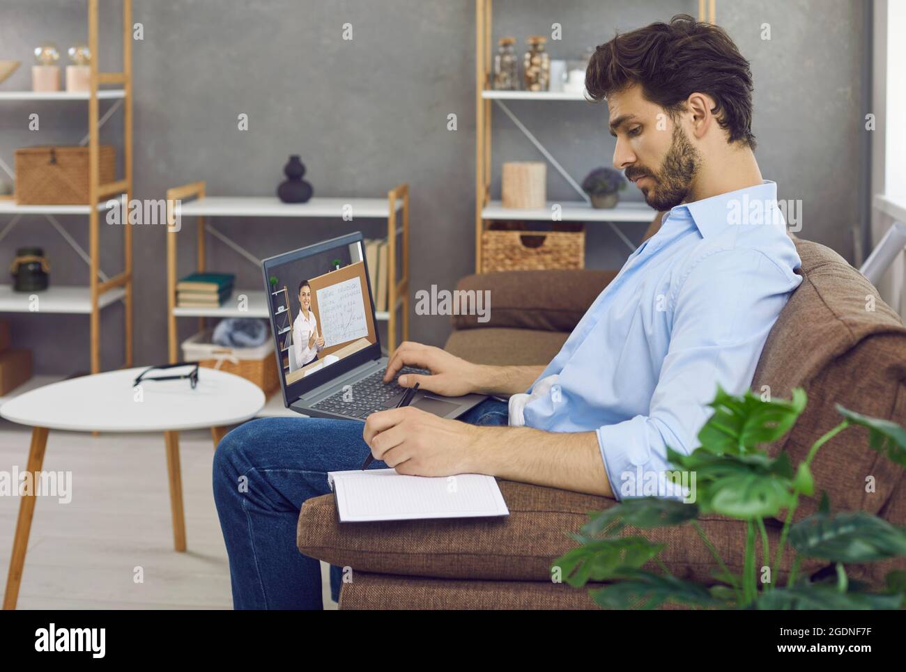 Young man sitting on sofa with laptop computer, having online class and ...