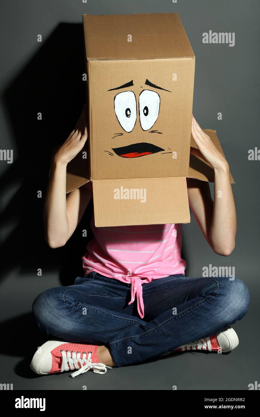 Woman with cardboard box on her head with sad face, on grey background ...