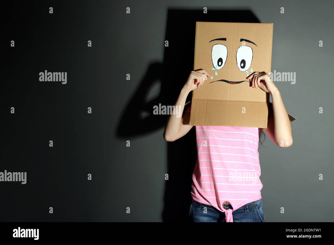Woman with cardboard box on her head with sad face, on grey background ...