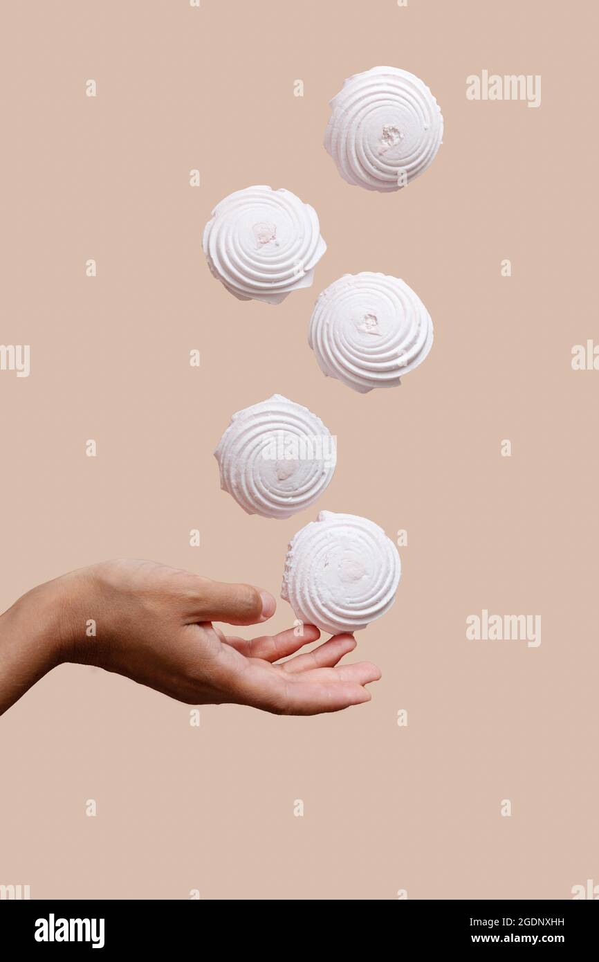 marshmallow floating in the air under hand against beige background ...