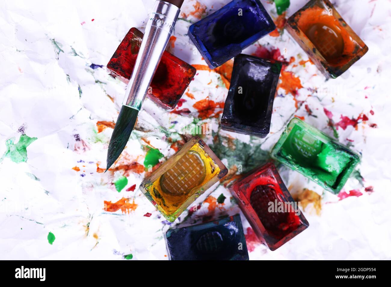 Watercolor paint cubes with brush and spilled paint on white paper ...