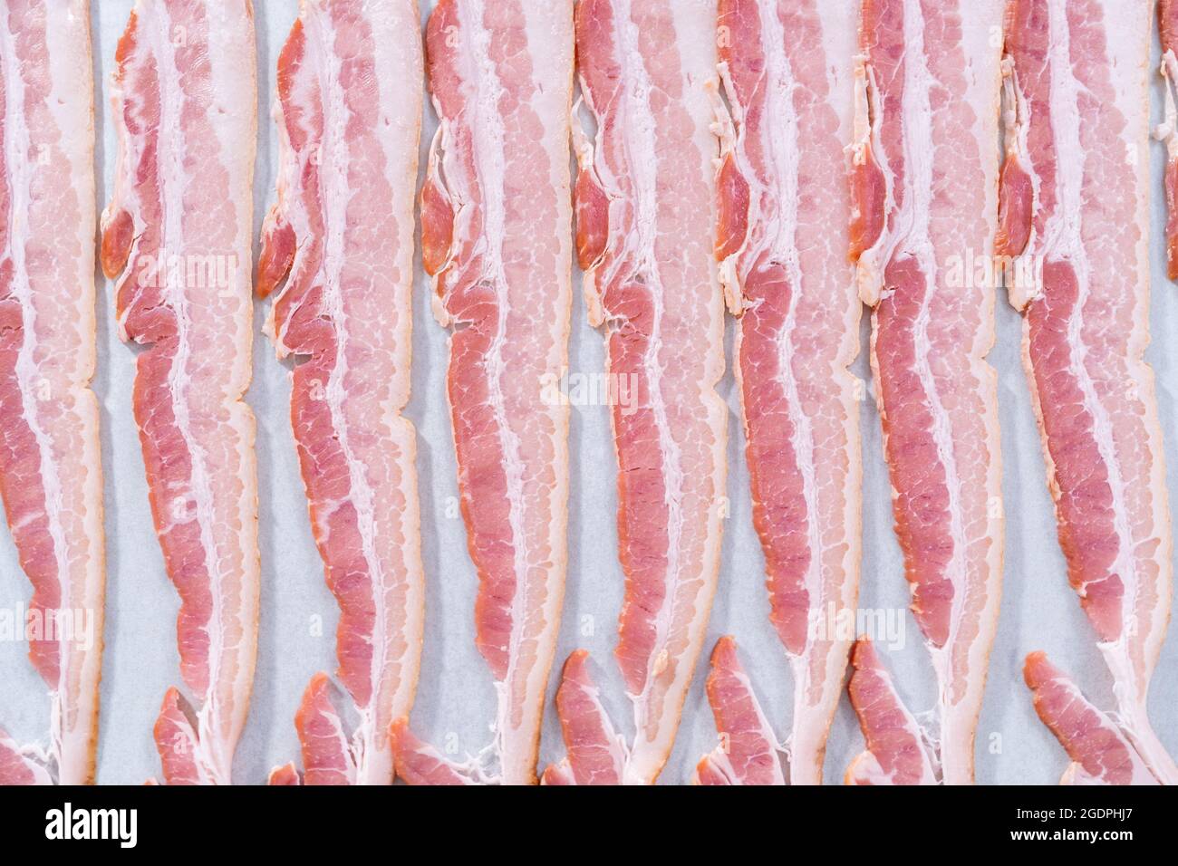 Uncooked bacon strips on a baking sheet with white parchment paper ...