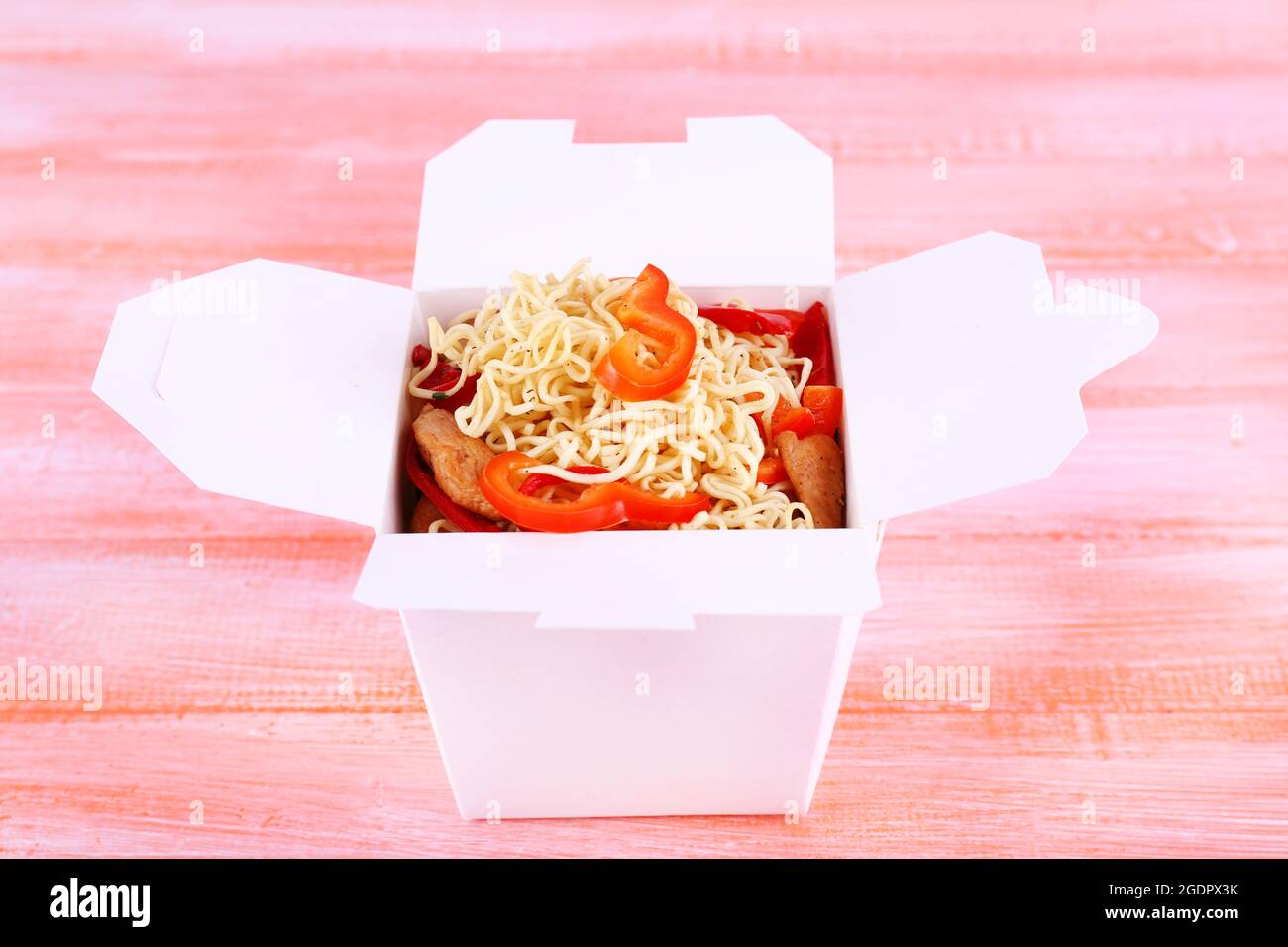 Chinese noodles with meat and pepper in takeaway box on pink background ...