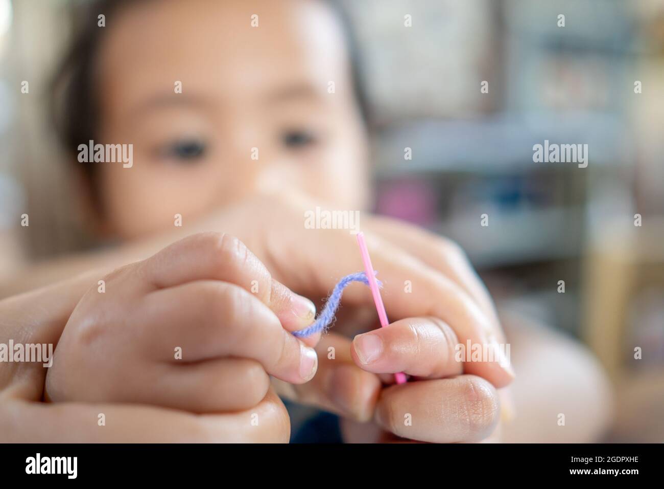 Cute Southeast Asian female child concentrated on thread the thread ...