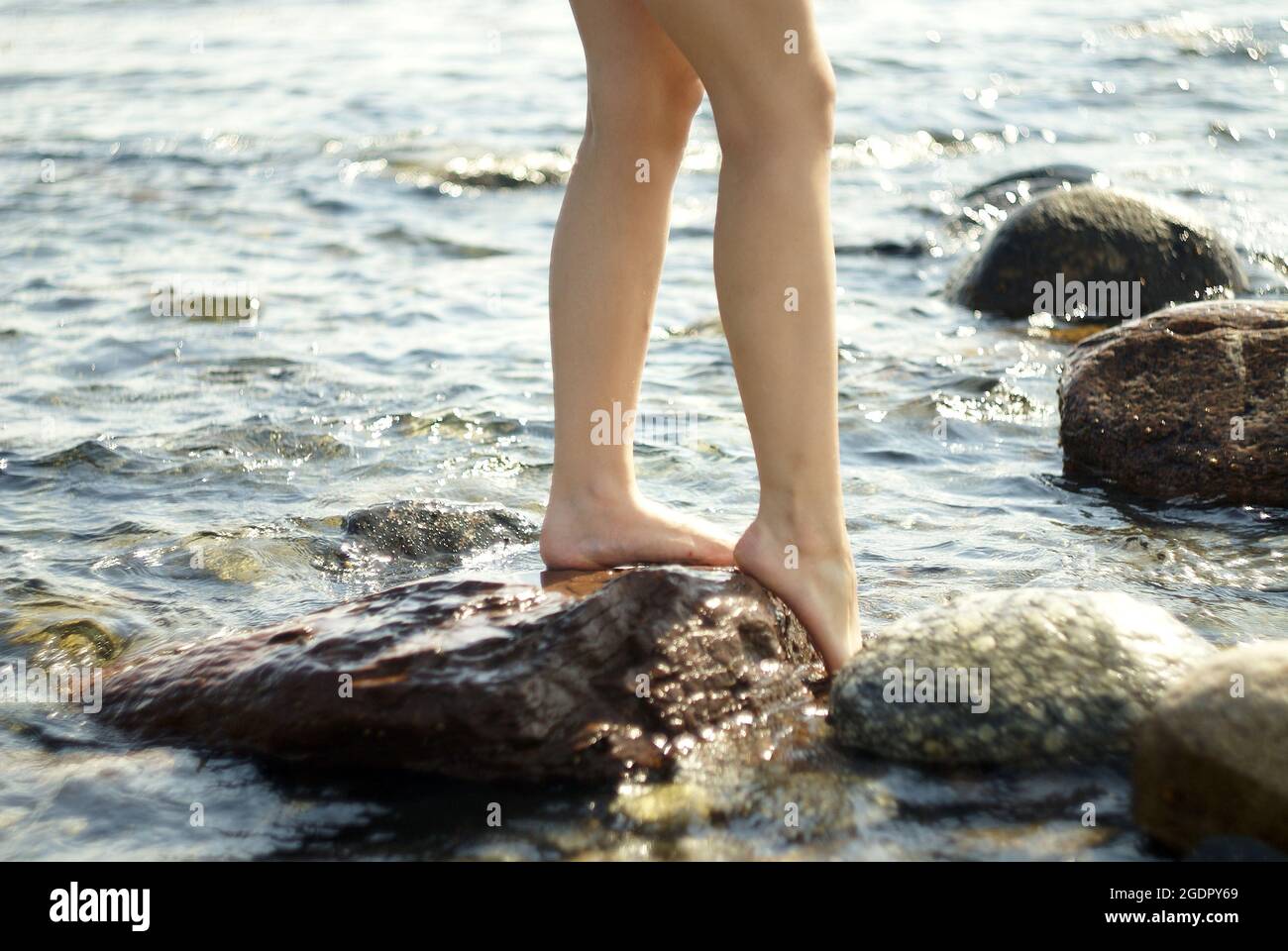 Closeup of a woman's legs as she walks on the rocks in an ocean on a ...