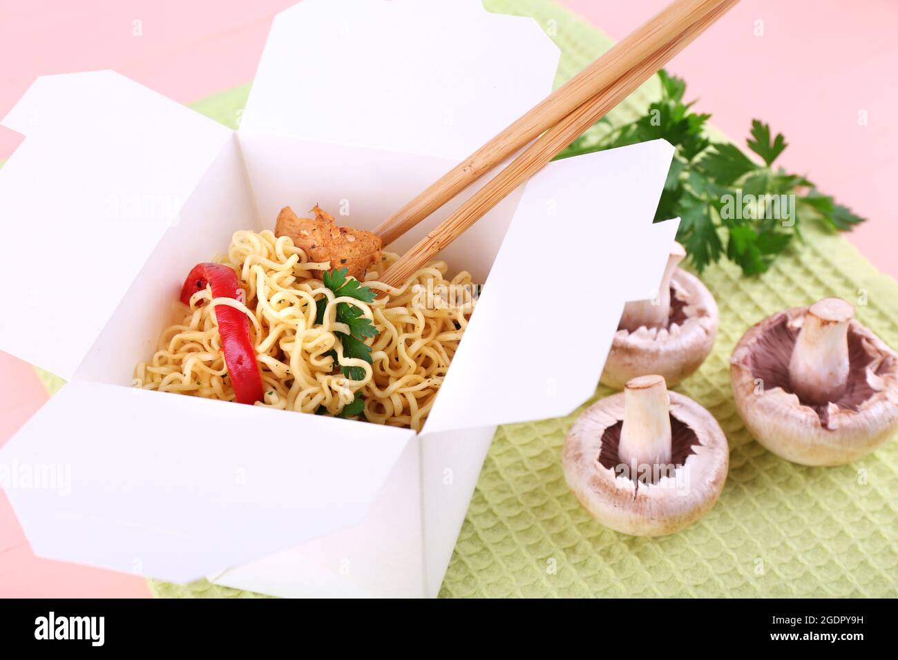 Chinese noodles and sticks in takeaway box on green napkin on pink ...